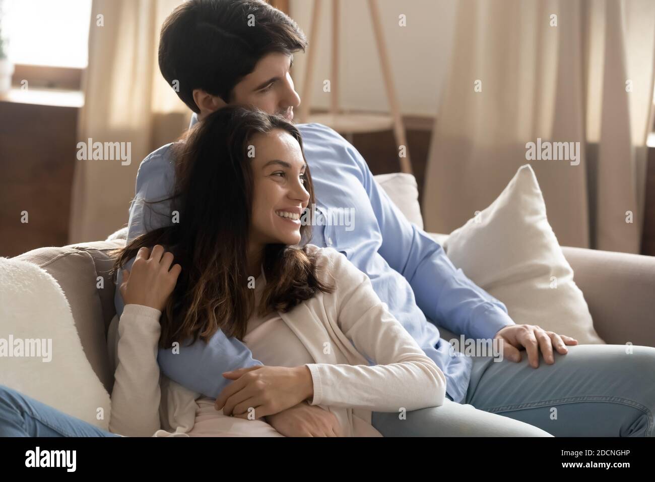 Calm peaceful young family couple embracing on couch watching tv Stock ...