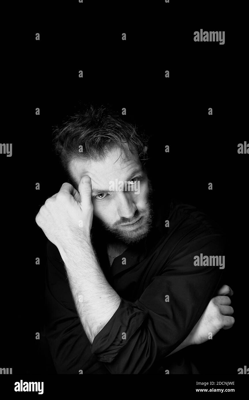 A man on a black background. He looks thoughtfully into the frame. A ...