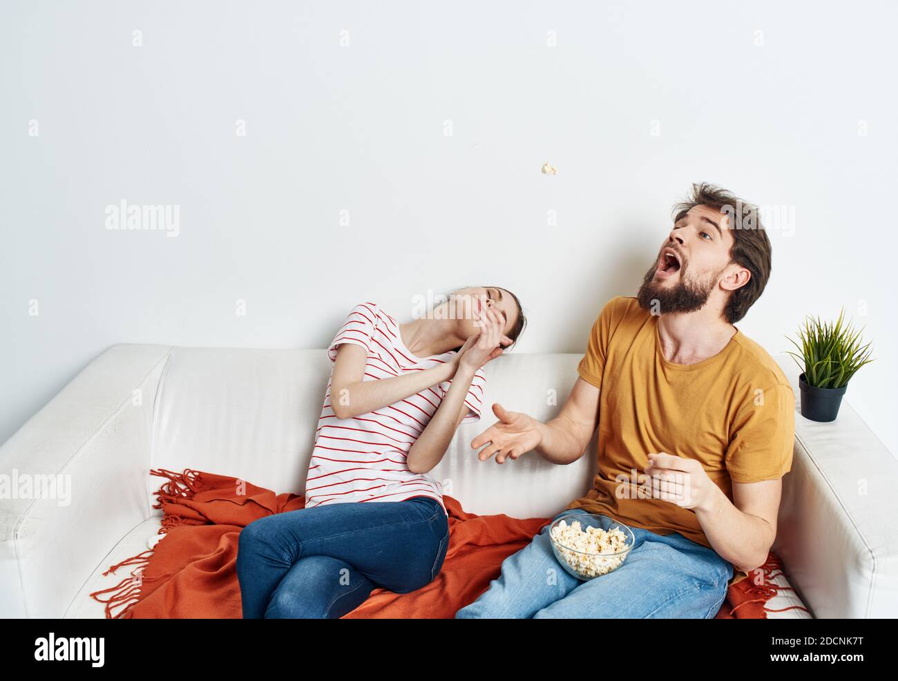 Fun man and energetic woman watching TV on the couch popcorn in a plate ...
