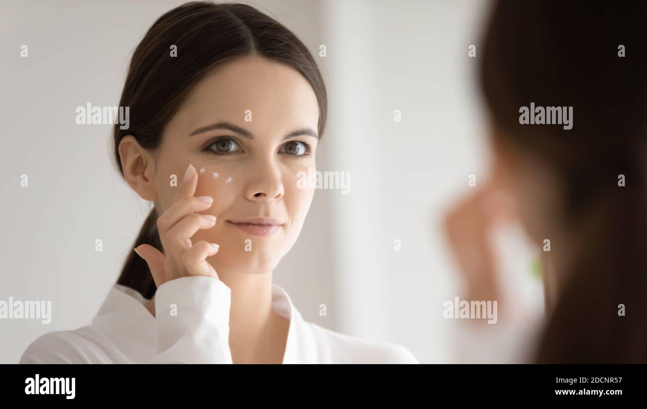 Concentrated woman doing domestic beauty procedures applying lotion on ...