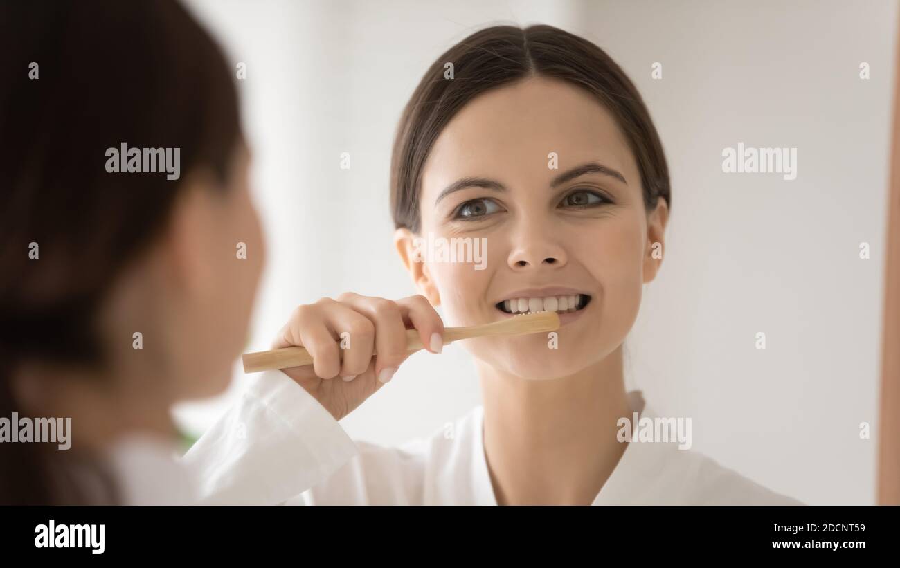 Happy female cleaning teeth in bathroom using bamboo eco toothbrush ...