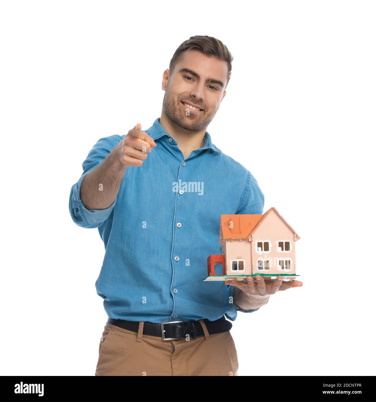 casual man holding a house model and pointing at the camera against ...