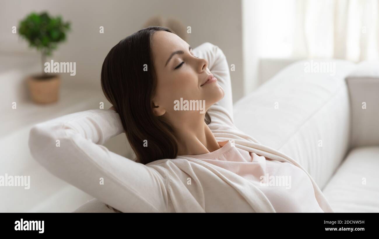 Tranquil millennial female napping on couch with hands behind head ...