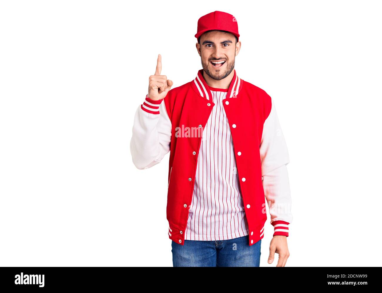 Young handsome man wearing baseball jacket and cap pointing finger up ...