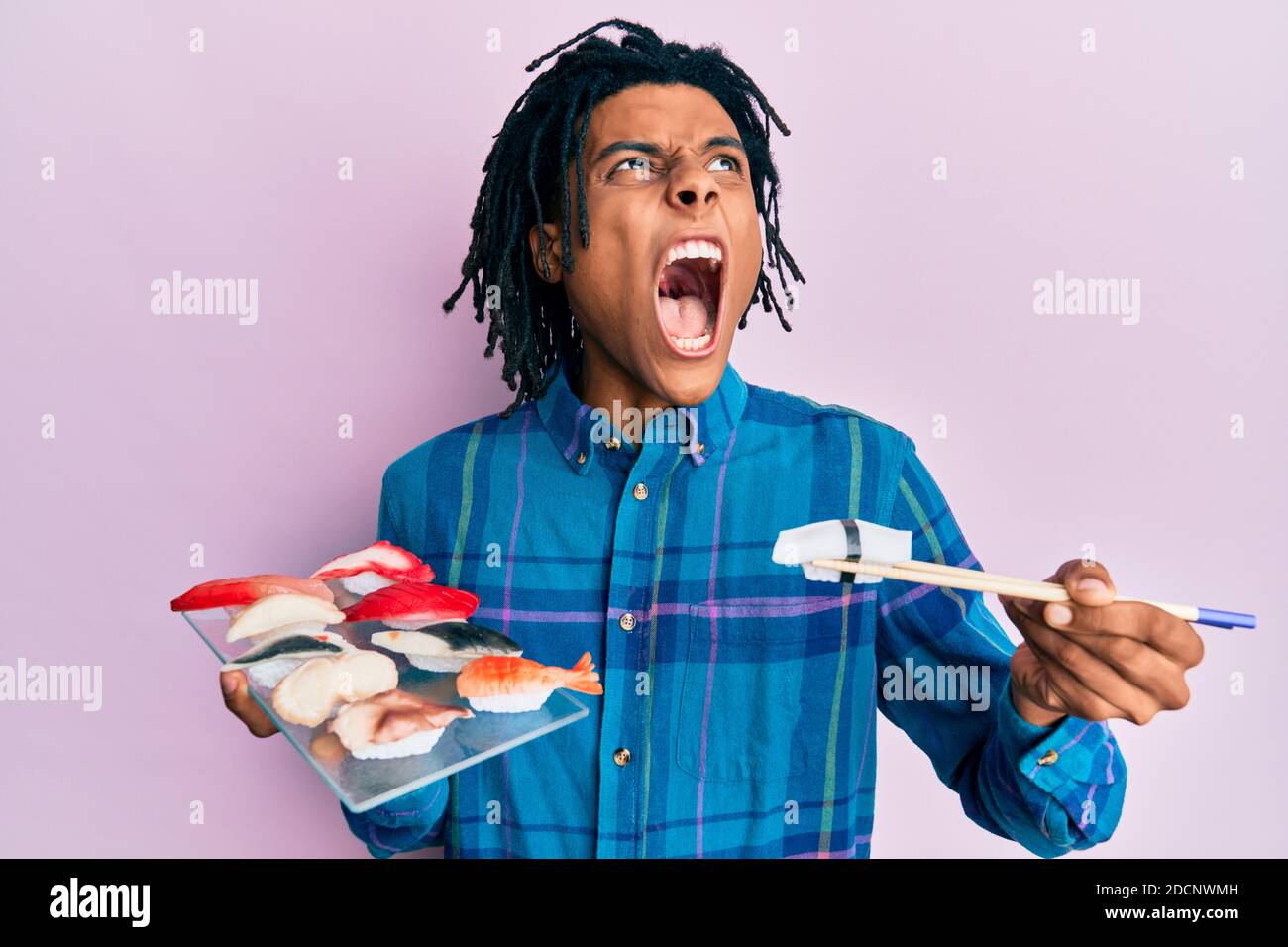 Young african american man eating sushi using chopsticks angry and mad ...