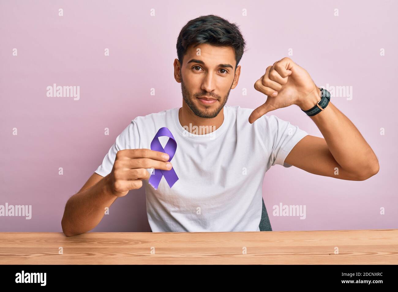 Young handsome man holding purple ribbon awareness with angry face ...
