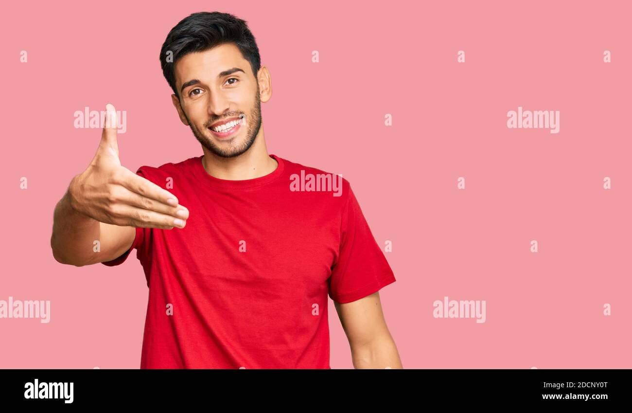 Young handsome man wearing casual red tshirt smiling friendly offering ...