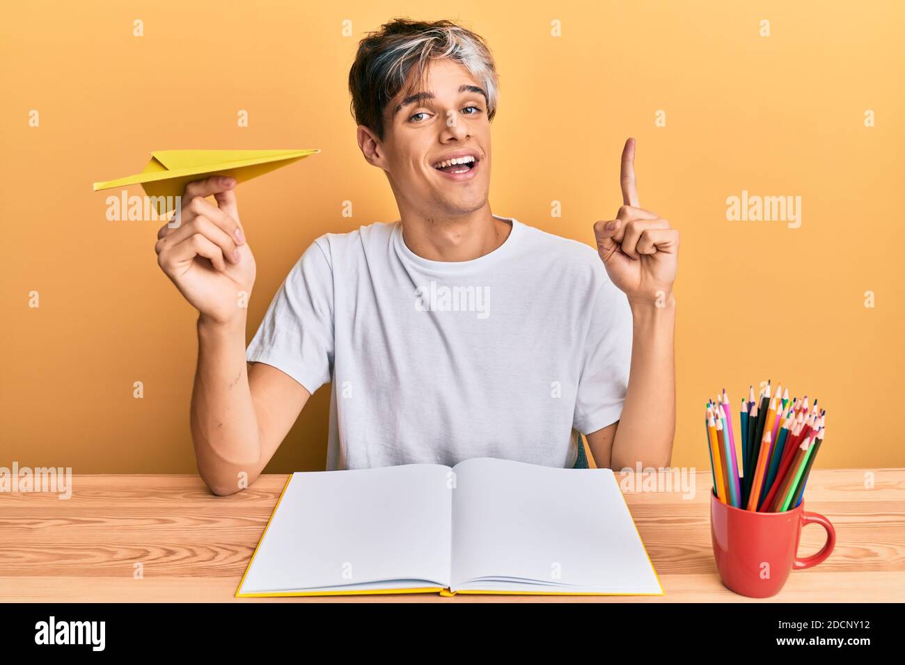 Young hispanic man studying and holding paper airplane sitting on the ...