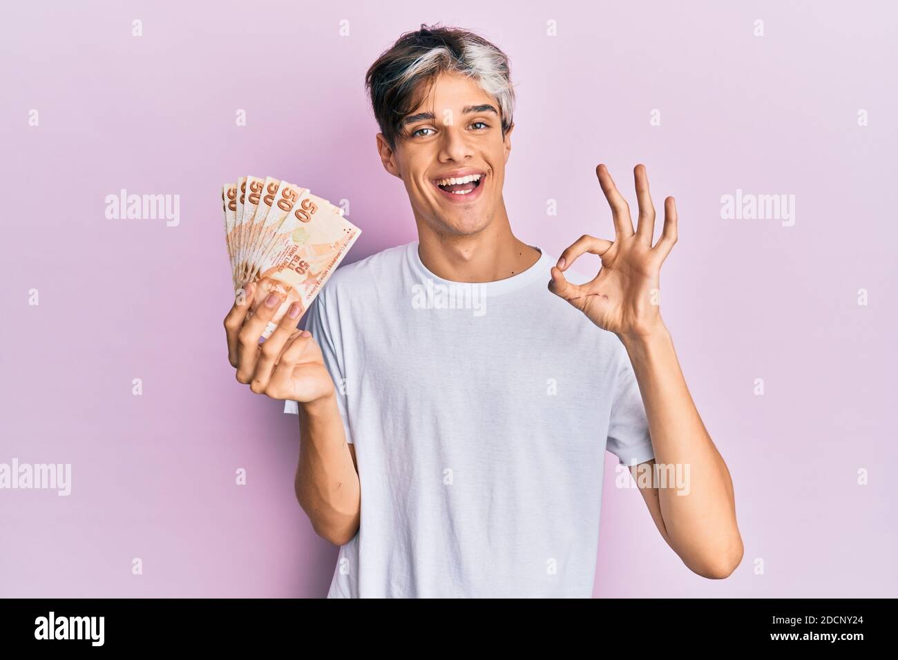 Young hispanic man holding 50 turkish lira banknotes doing ok sign with ...