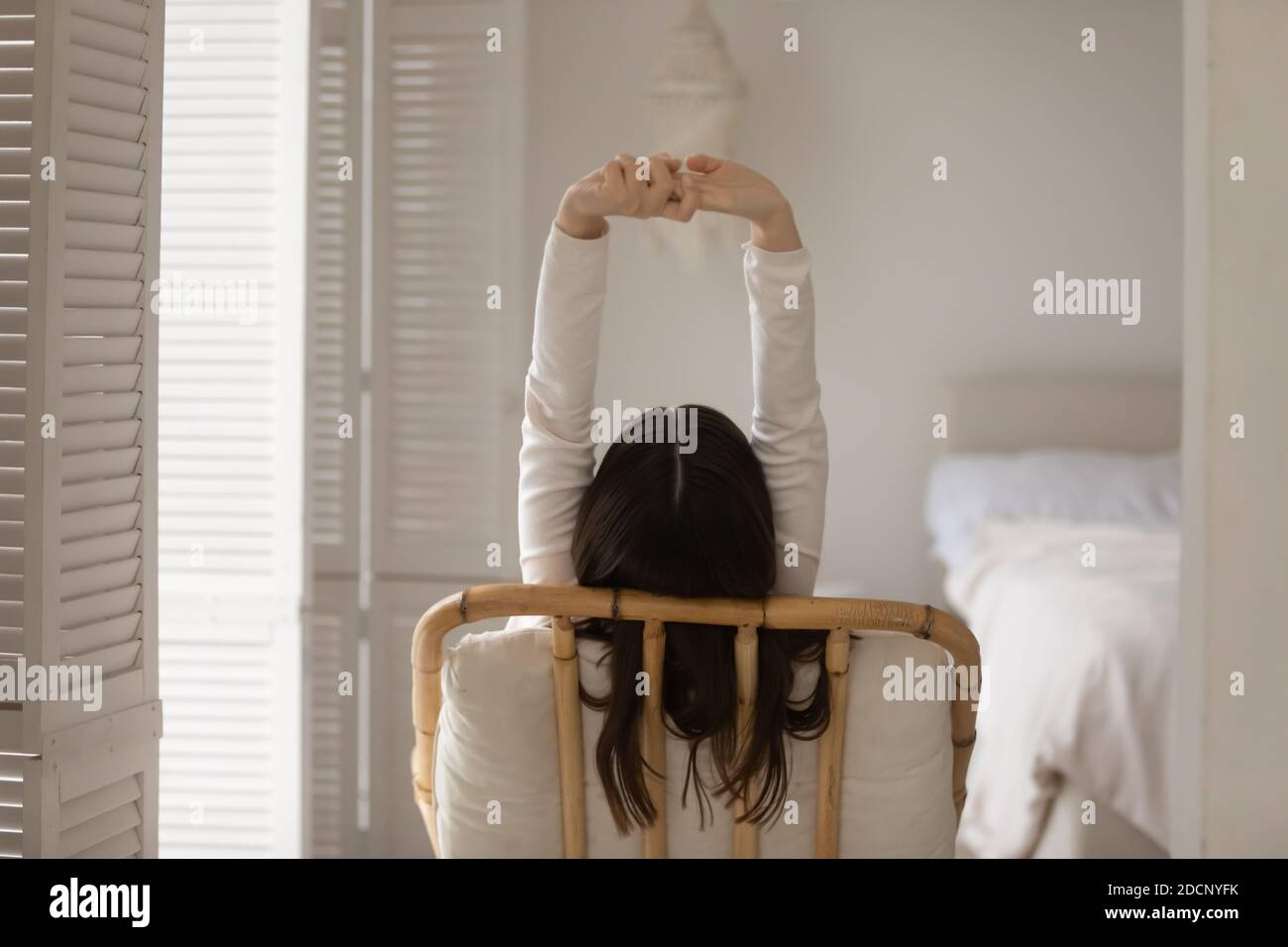 Relaxed young woman stretching arms sitting in armchair at bedroom ...
