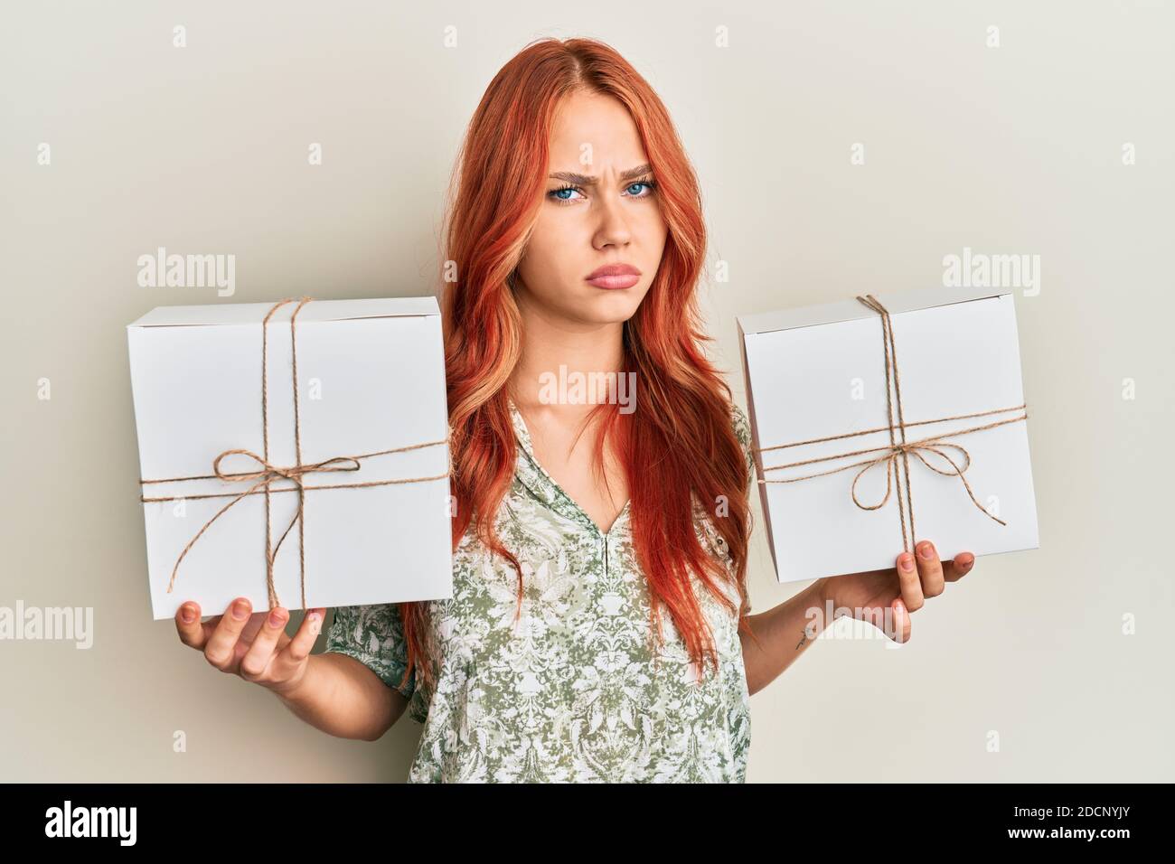 Young redhead woman holding gifts skeptic and nervous, frowning upset ...