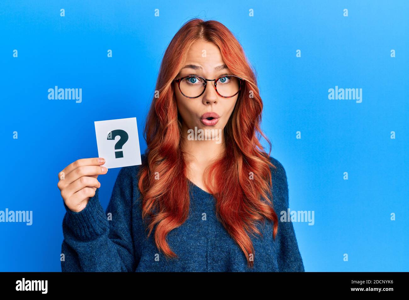 Young beautiful redhead woman holding question mark scared and amazed ...