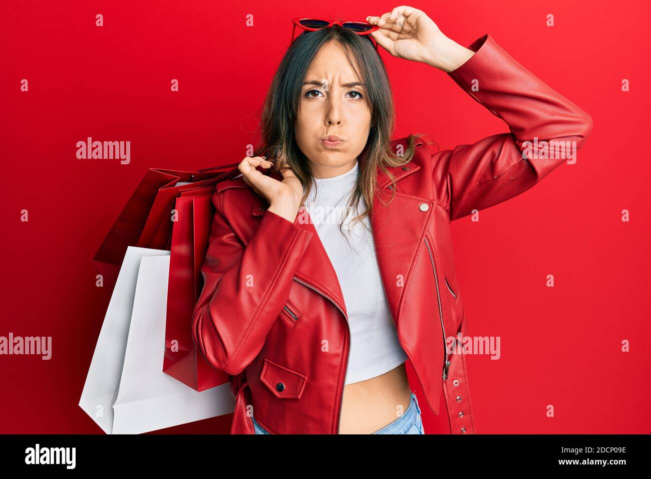 Young brunette woman holding shopping bags skeptic and nervous ...