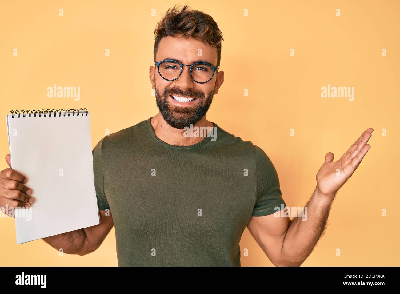 Young hispanic man wearing glasses holding notebook celebrating victory ...