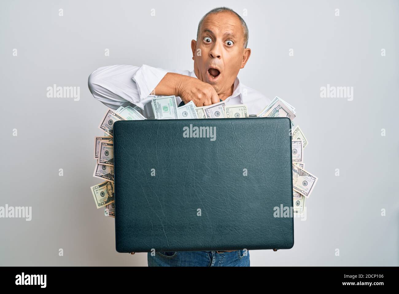 Handsome senior man holding briefcase full of dollars in shock face ...
