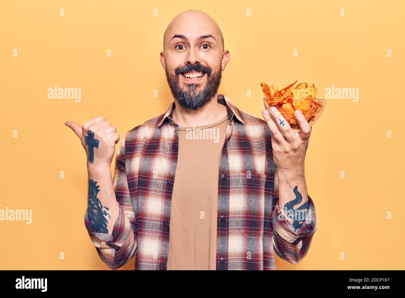 Young handsome man holding nachos potato chips pointing thumb up to the ...