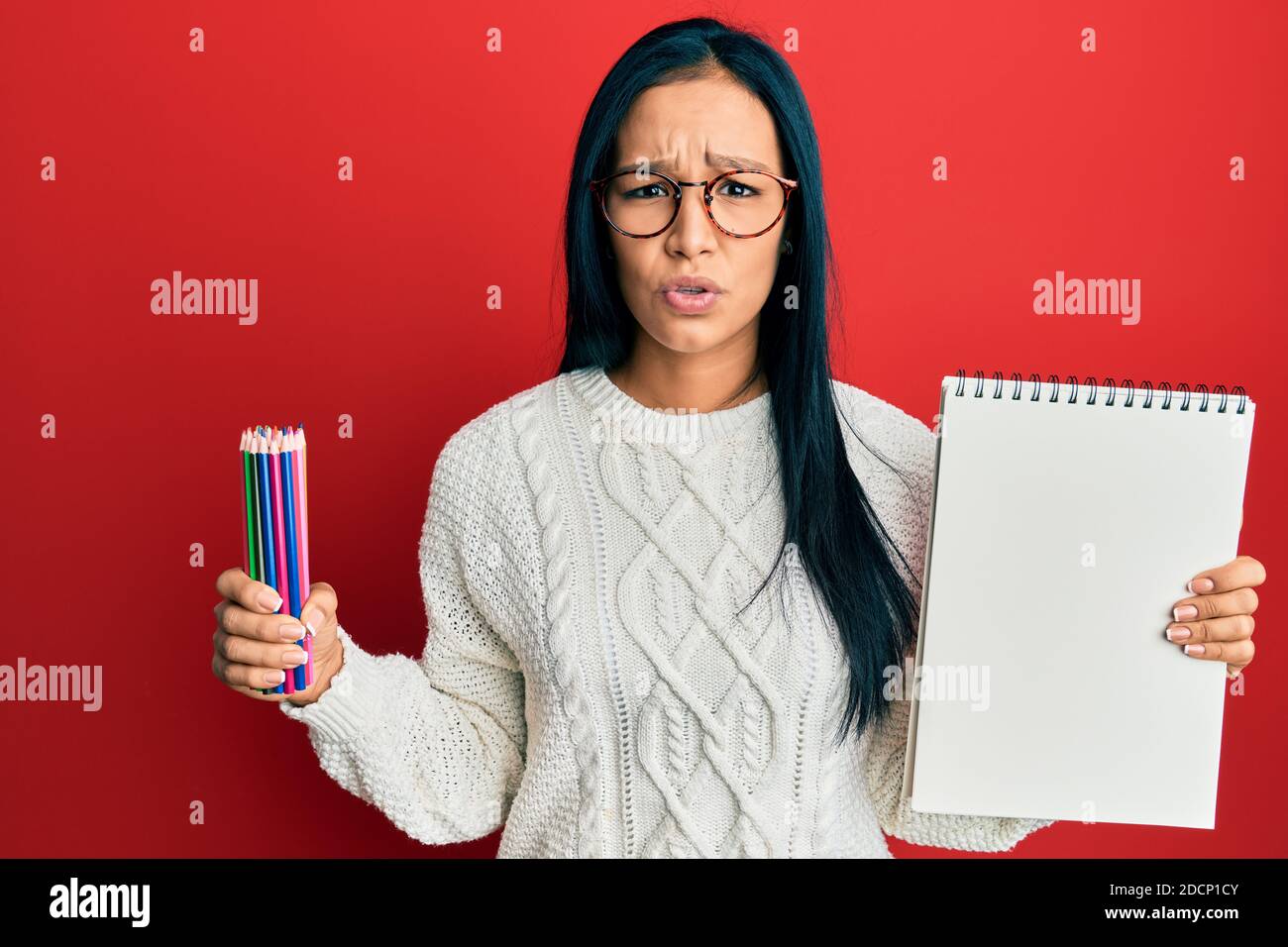Beautiful hispanic woman holding canvas book and colored pencils in ...
