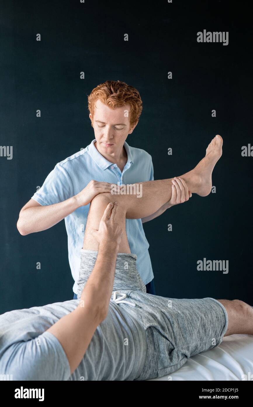 Contemporary clinician holding leg bent in knee of his patient lying on ...