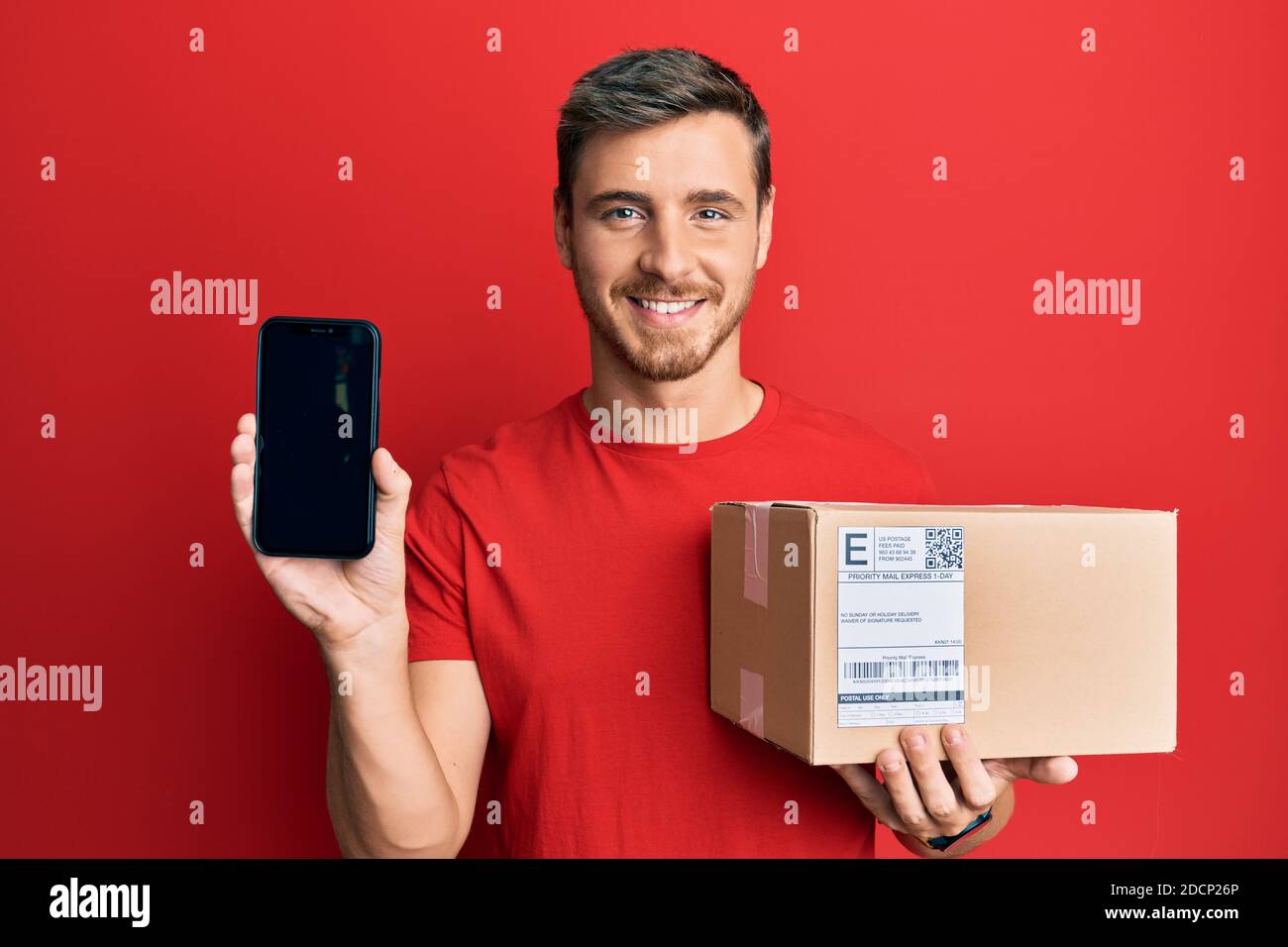 Handsome caucasian man holding delivery package and showing smartphone ...