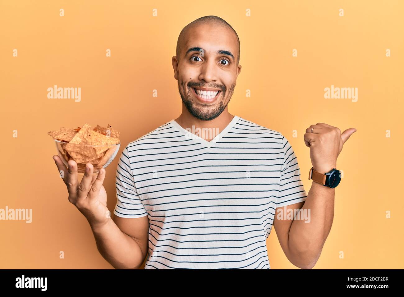 Hispanic adult man holding nachos potato chips pointing thumb up to the ...