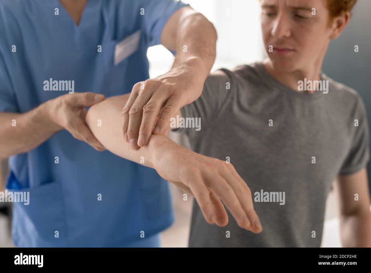Hands of mature clinician in blue uniform supporting bent arm of young ...