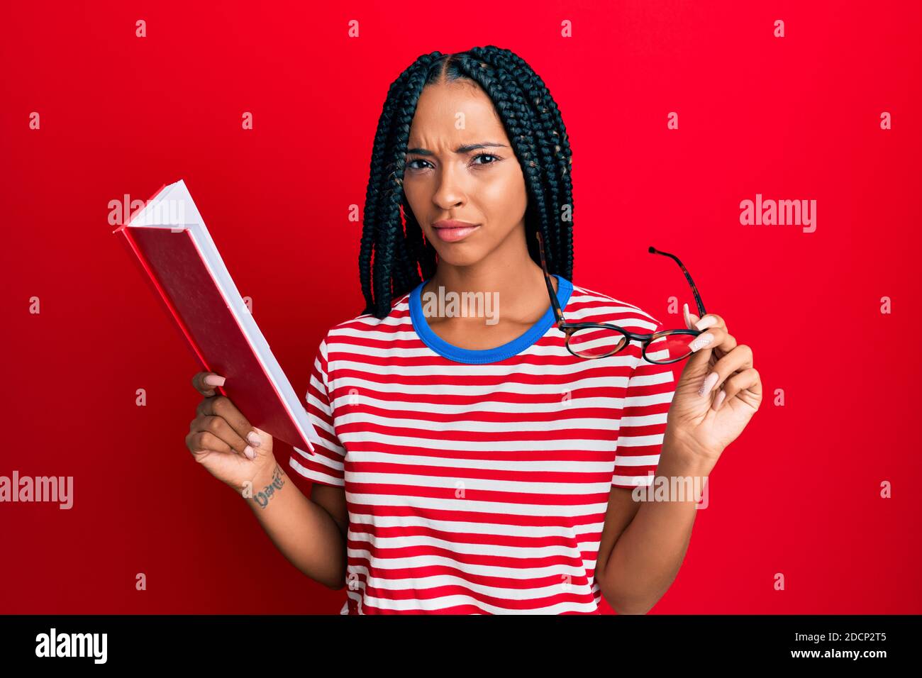 Beautiful hispanic woman reading a book with glasses skeptic and ...