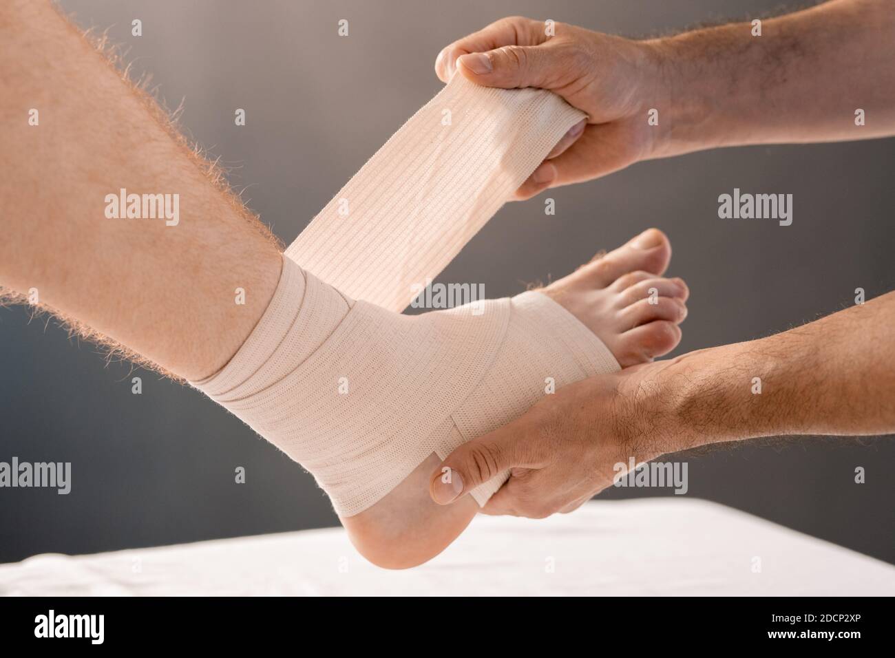 Hands of clinician wrapping foot and leg of young male patient with ...