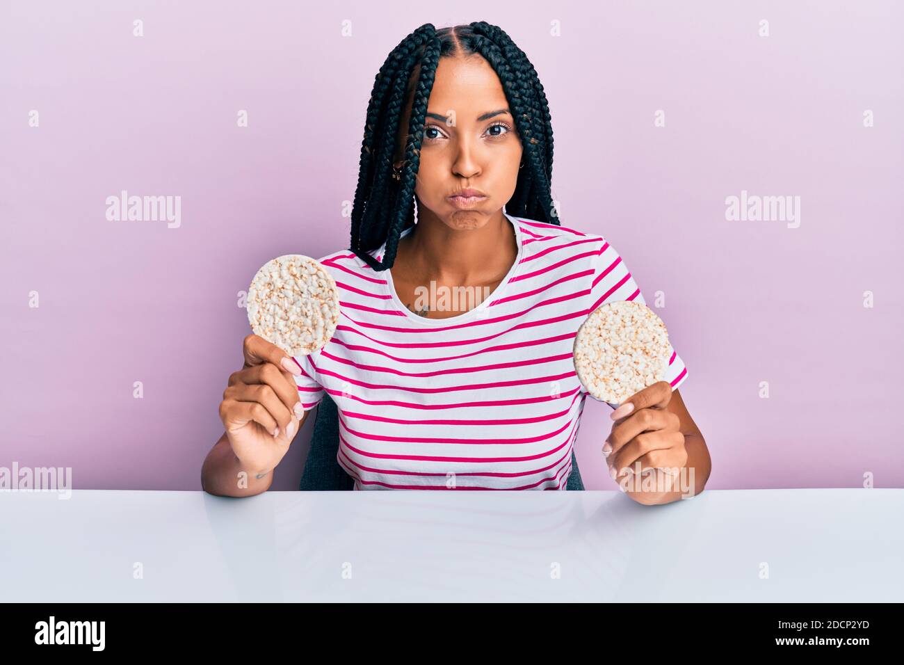 Beautiful hispanic woman eating healthy rice crackers puffing cheeks ...