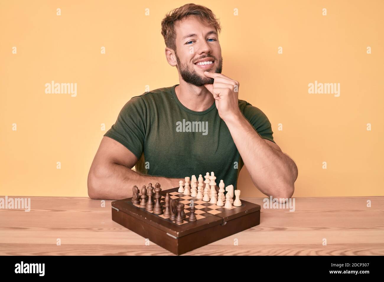 Young caucasian man playing chess sitting on the table smiling looking ...