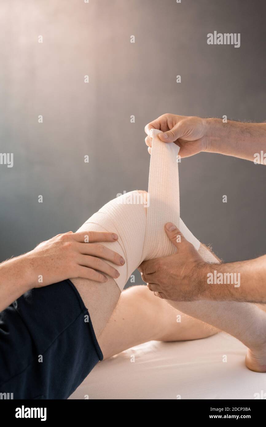 Hands of clinician wrapping right knee of sick man with flexible ...