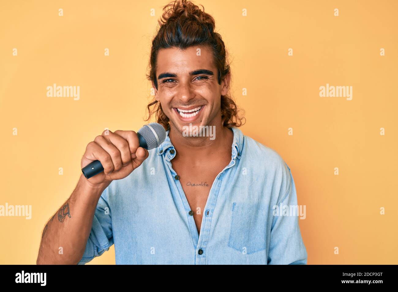 Young hispanic man singing song using microphone looking positive and ...