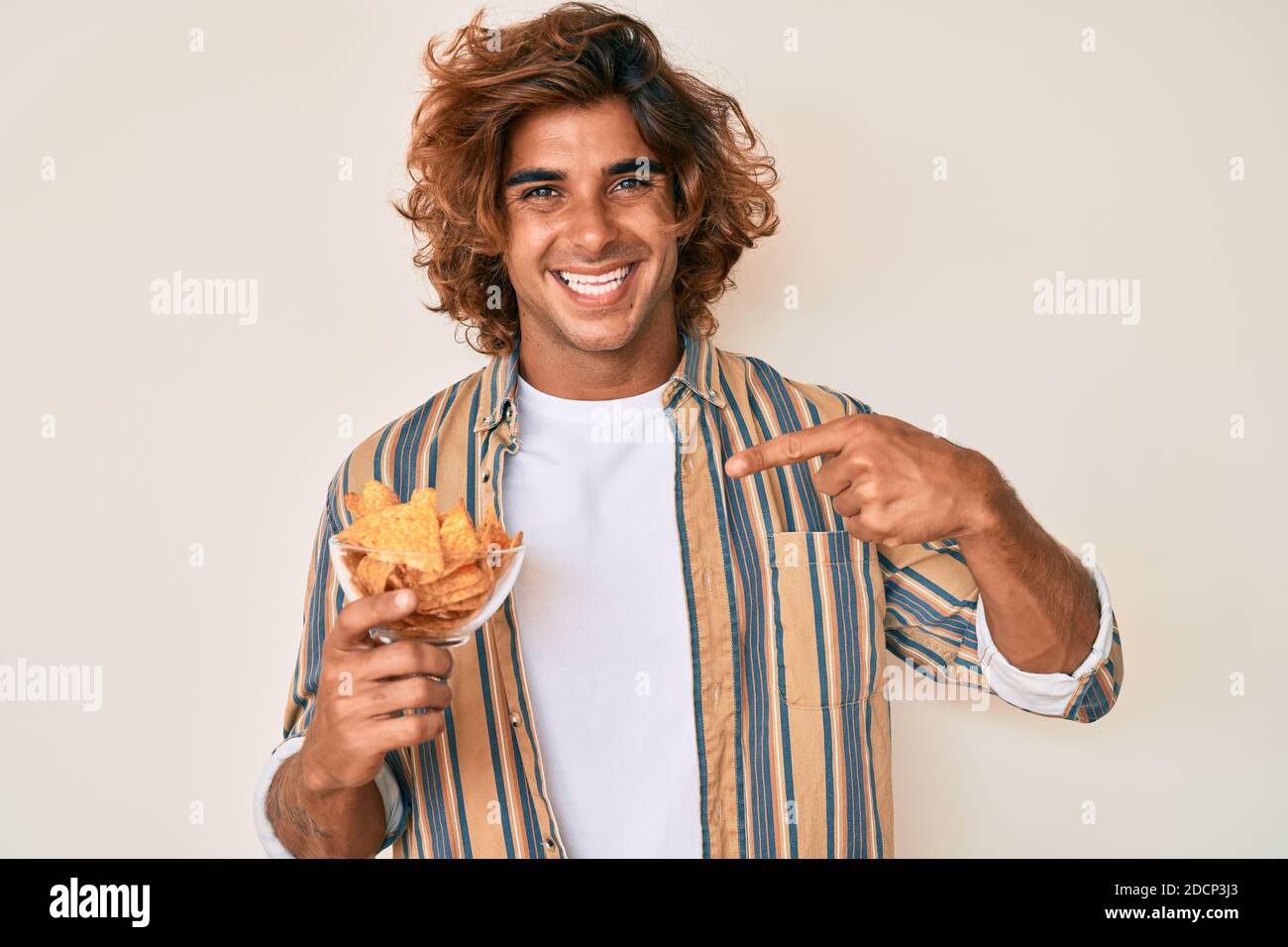 Young hispanic man holding nachos potato chips smiling happy pointing ...