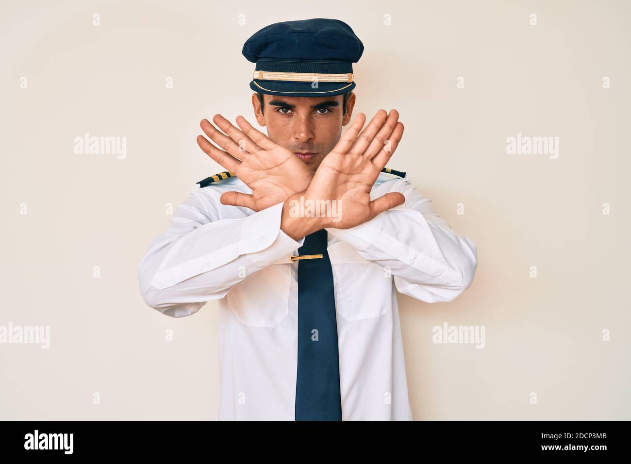 Young hispanic man wearing airplane pilot uniform rejection expression ...