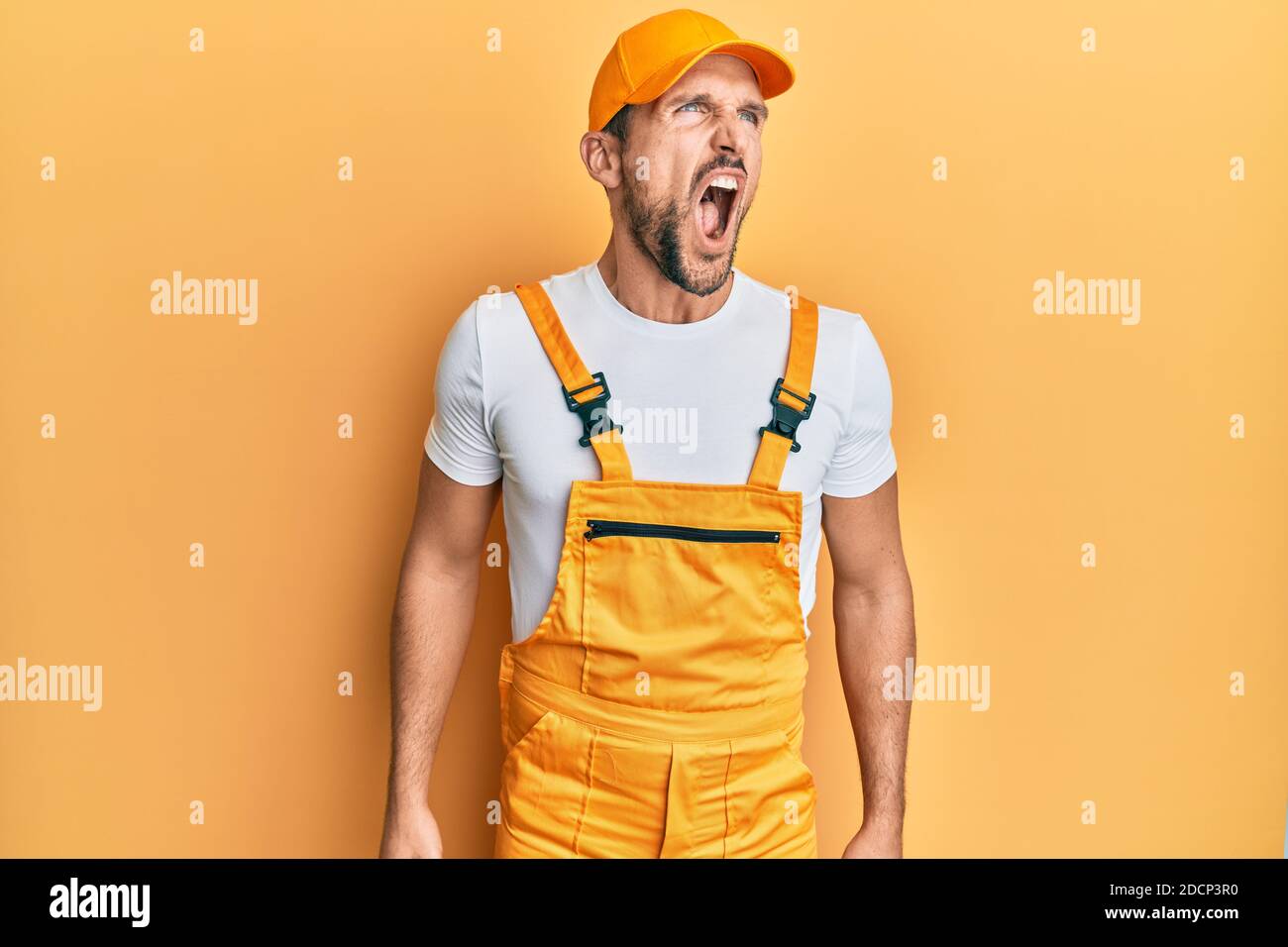 Young handsome man wearing handyman uniform over yellow background ...