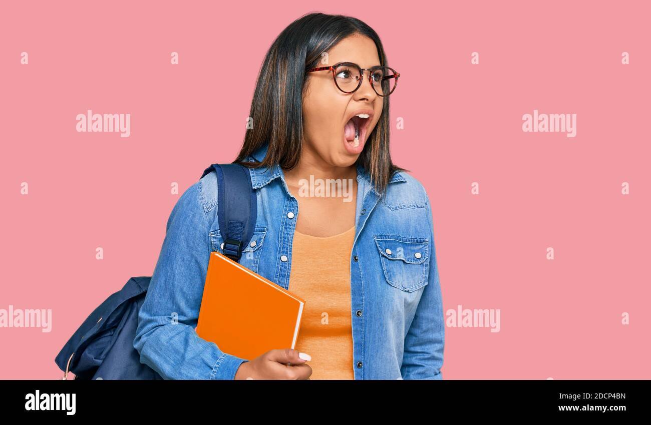 Young latin girl wearing student backpack and holding books angry and ...