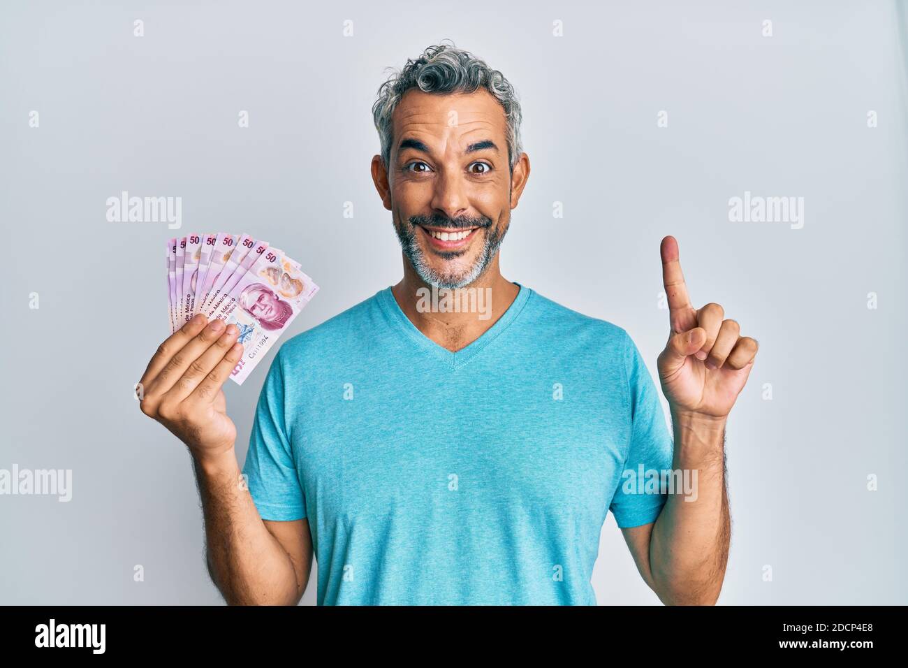 Middle age grey-haired man holding mexican pesos smiling with an idea ...