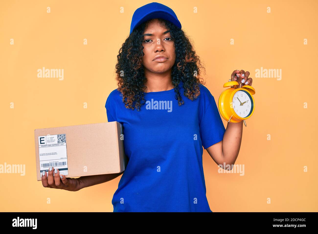 Young african american woman holding delivery package and alarm clock ...
