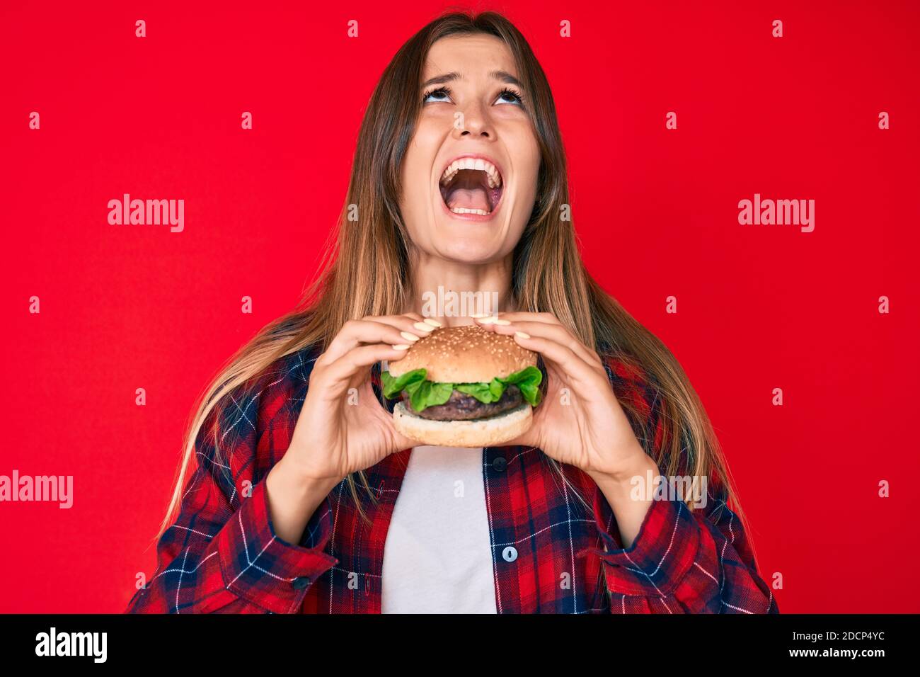 Beautiful caucasian woman eating a tasty classic burger angry and mad ...