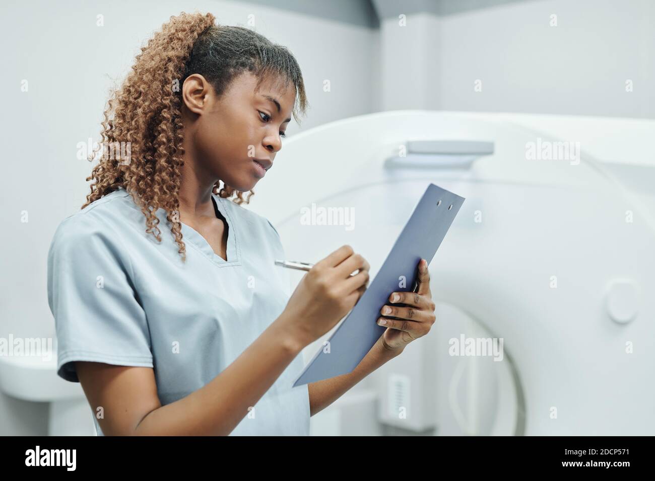 Pretty nurse of African ethnicity in uniform making notes in medical ...