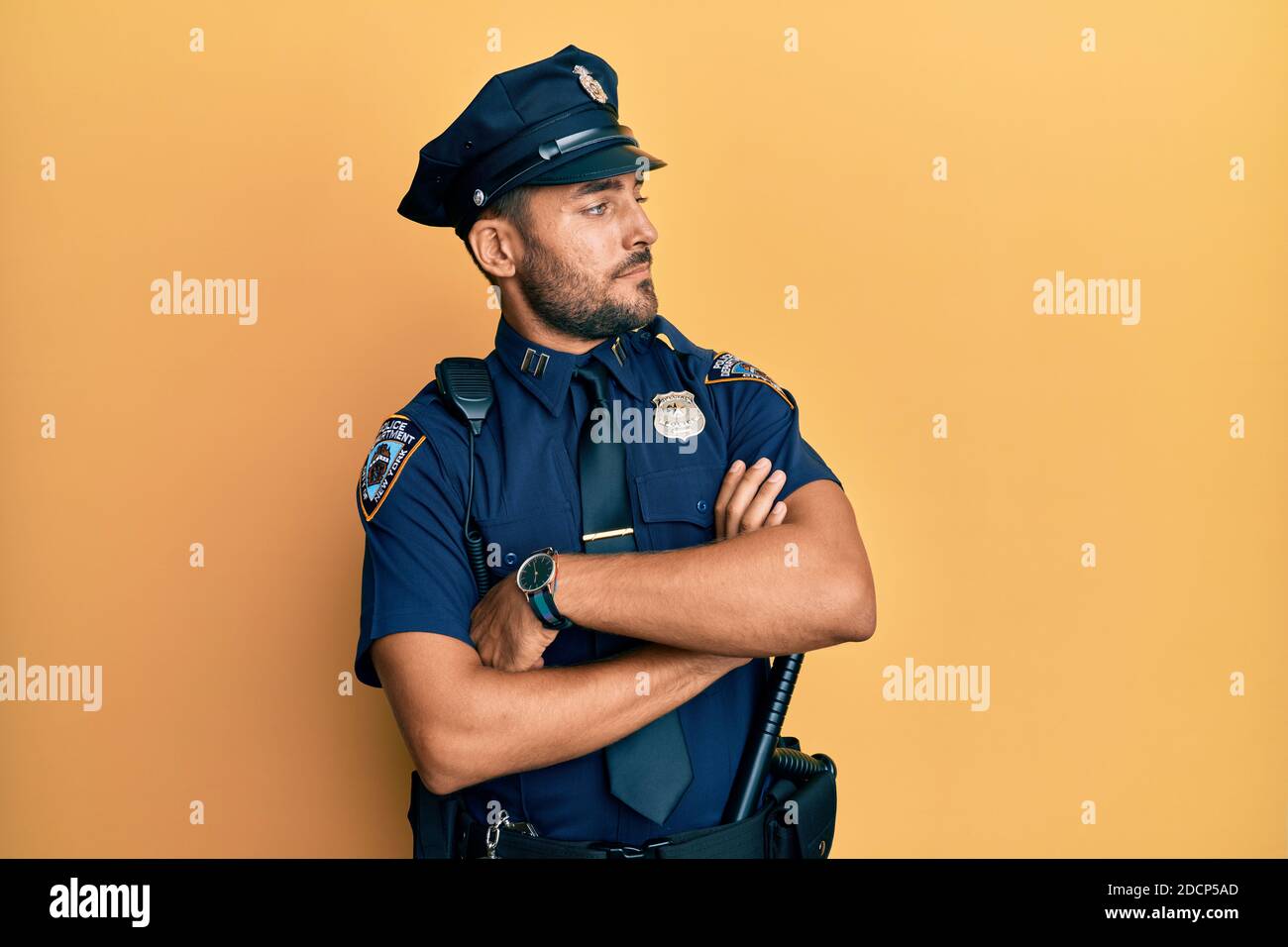 Handsome hispanic man wearing police uniform looking to the side with ...