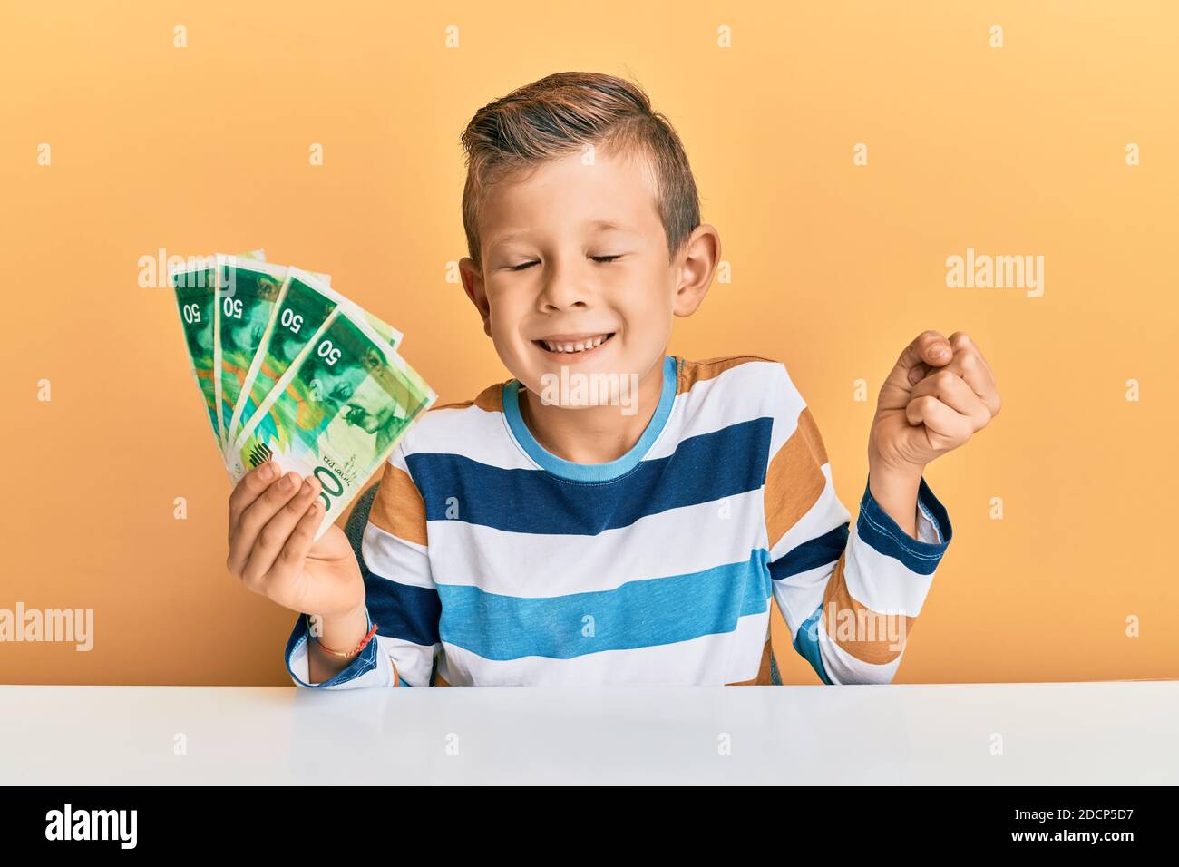 Adorable caucasian kid holding israel 50 shekels sitting on the table ...