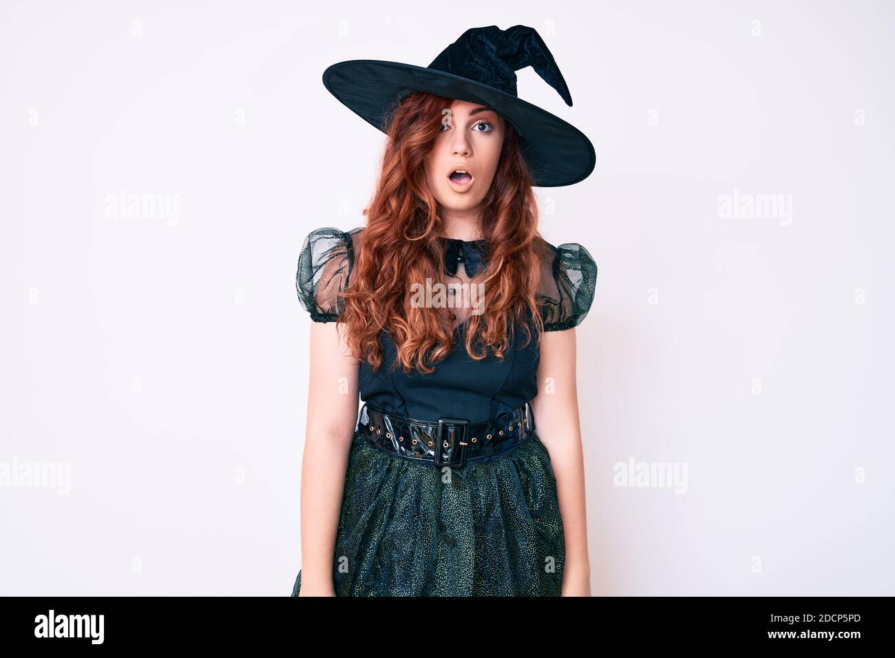 Young beautiful woman wearing witch halloween costume in shock face ...