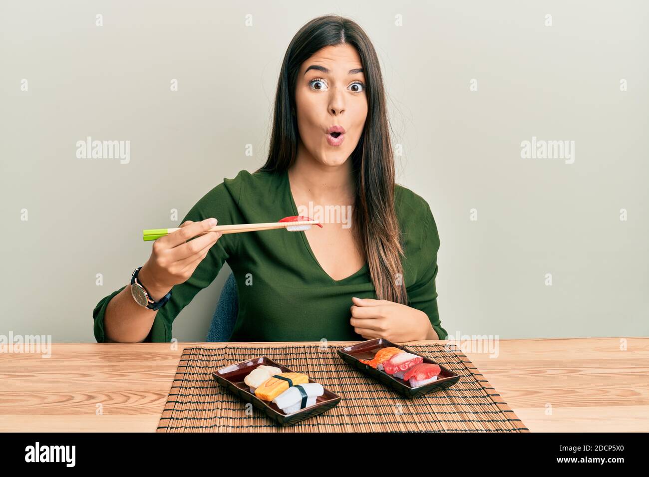 Young brunette woman eating sushi sitting on the table scared and ...