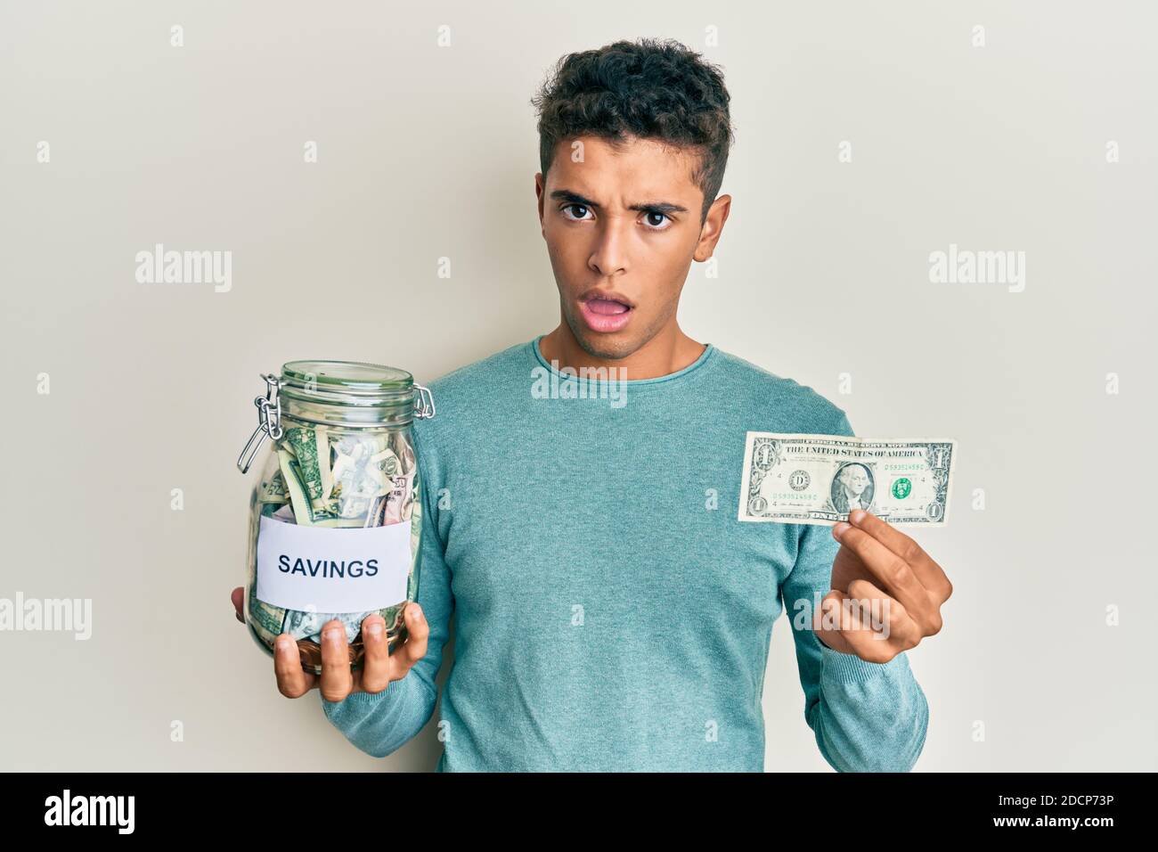 Young handsome african american man holding jar with savings in shock ...