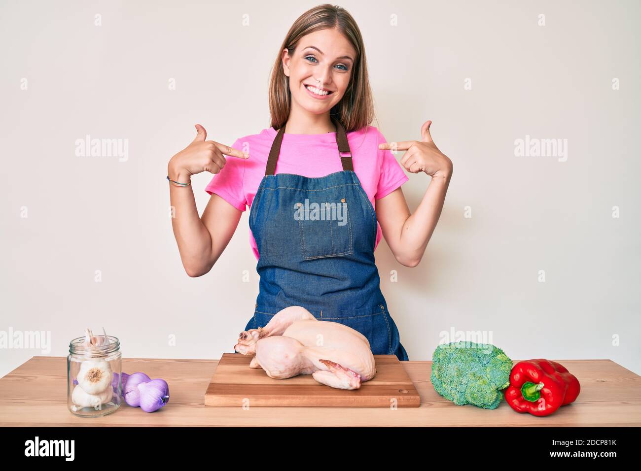 Young blonde girl wearing cook apron and holding chicken looking ...