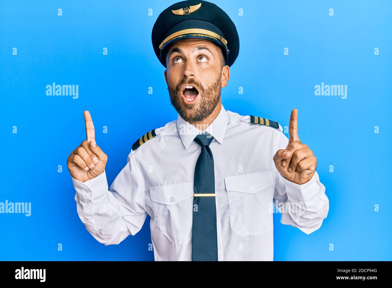 Handsome man with beard wearing airplane pilot uniform amazed and ...