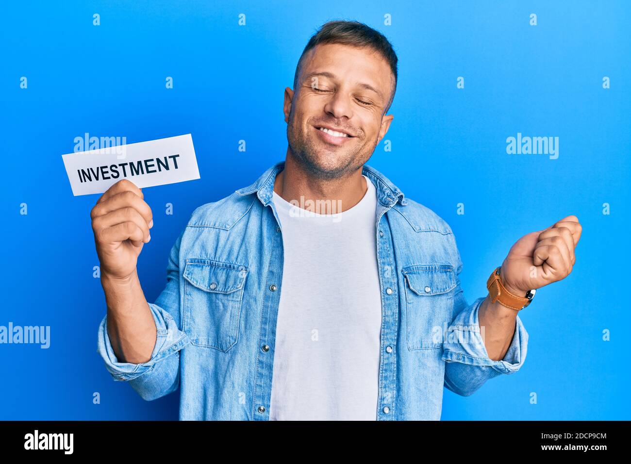 Handsome muscle man holding investment word on paper screaming proud ...