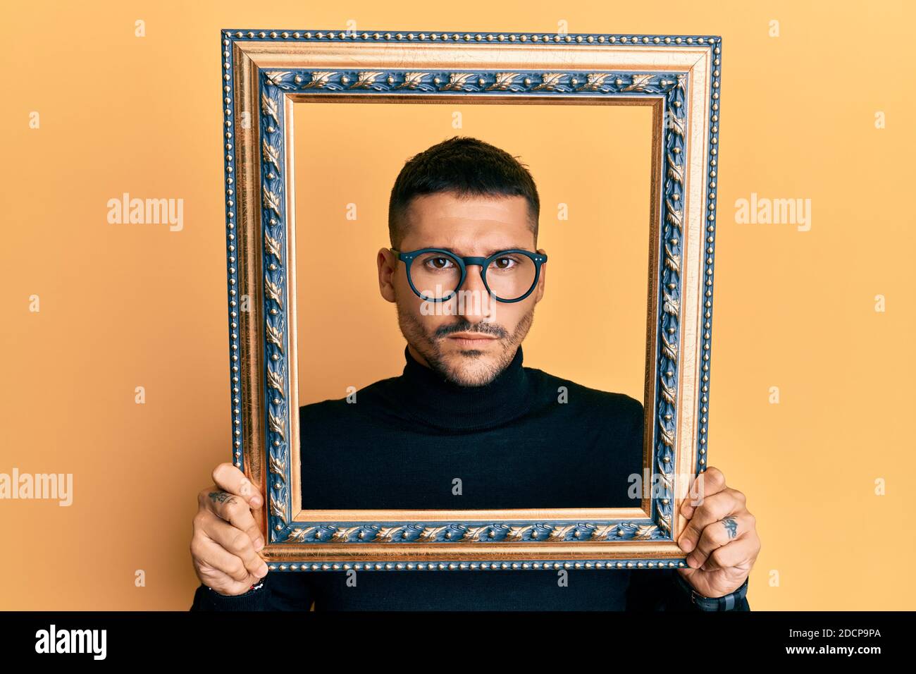Handsome man with tattoos holding empty frame skeptic and nervous ...