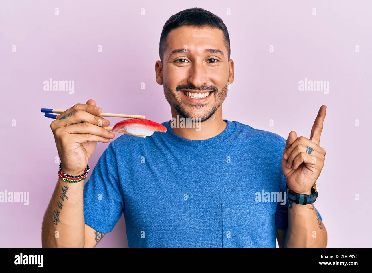Handsome man with tattoos eating tuna sushi using chopsticks smiling ...