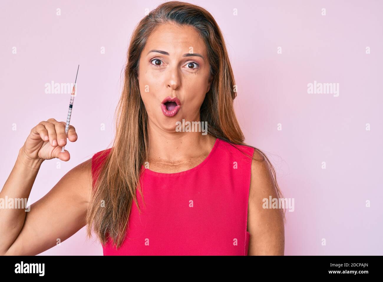 Middle age hispanic woman holding syringe scared and amazed with open ...